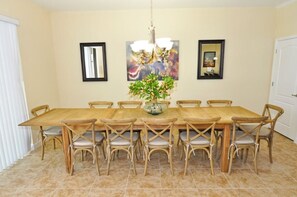 Uma sala de jantar com uma mesa de madeira retangular cercada por seis cadeiras, um lustre e duas obras de arte emolduradas nas paredes.