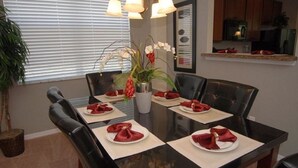 Uma sala de jantar com mesa de vidro, guardanapos vermelhos e um vaso de flores.