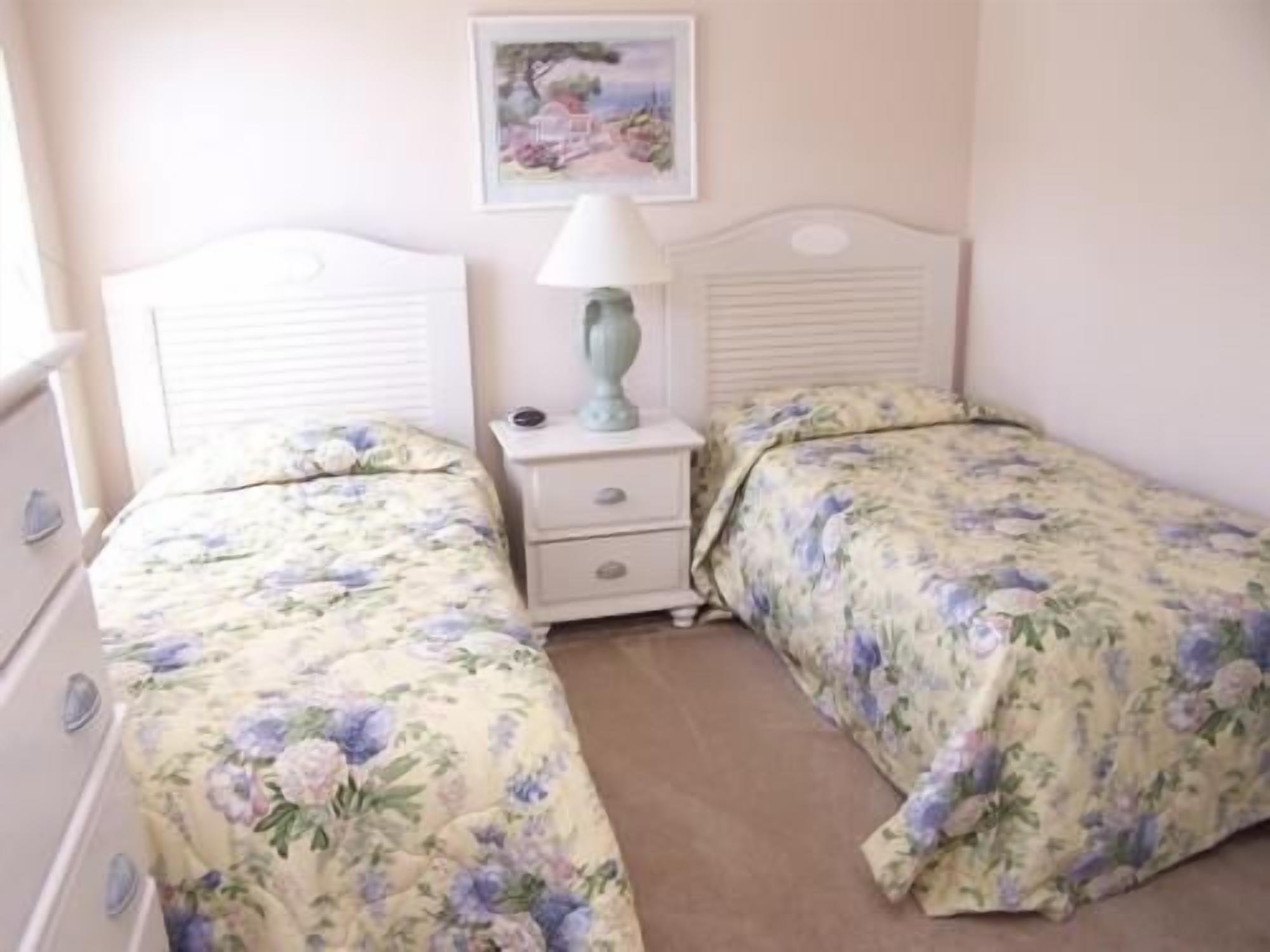 Um quarto com duas camas de solteiro, uma mesa de cabeceira com abajur e um quadro na parede.
