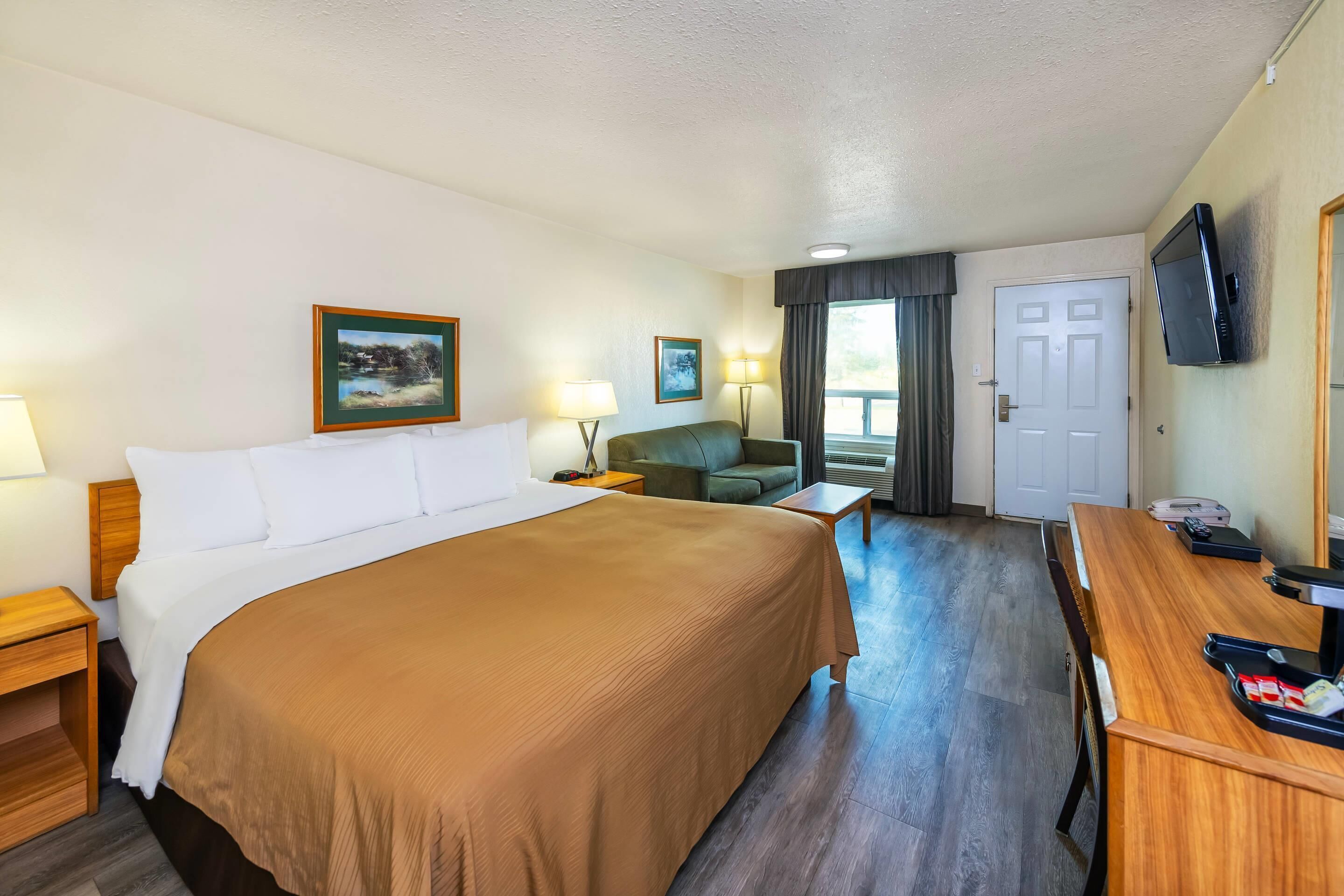 Quarto de hotel com uma cama grande, uma escrivaninha, uma cadeira, uma televisão e uma porta.