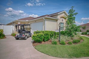 Uma casa residencial com garagem, um carrinho de golfe e paisagismo bem cuidado.