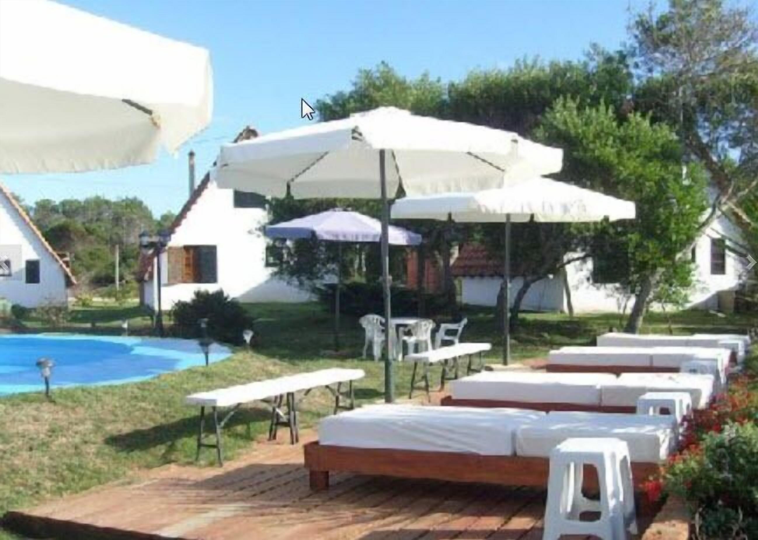 Uma área à beira da piscina com espreguiçadeiras e guarda-sóis, piscina e gramado.