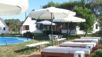 Uma área à beira da piscina com espreguiçadeiras e guarda-sóis, piscina e gramado.