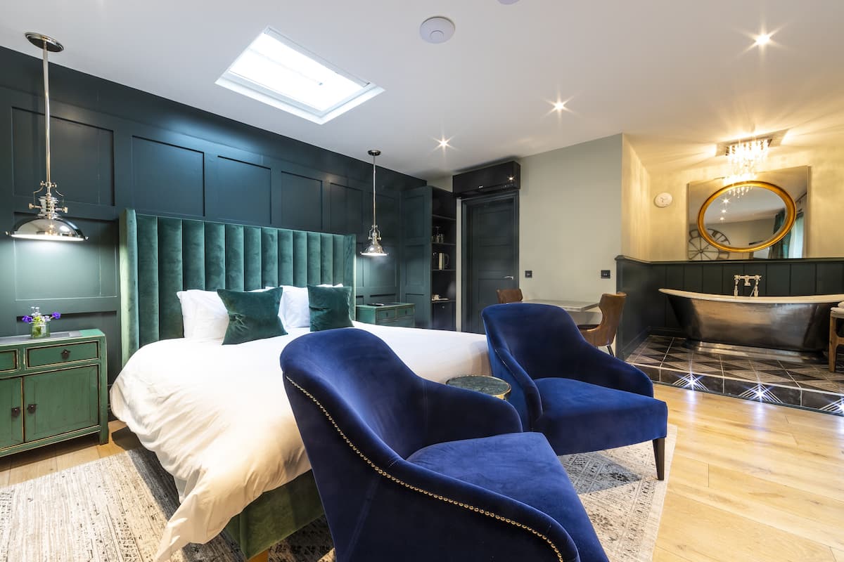 Quarto moderno com uma cama grande, duas poltronas azuis, uma toucador com espelho e uma banheira.