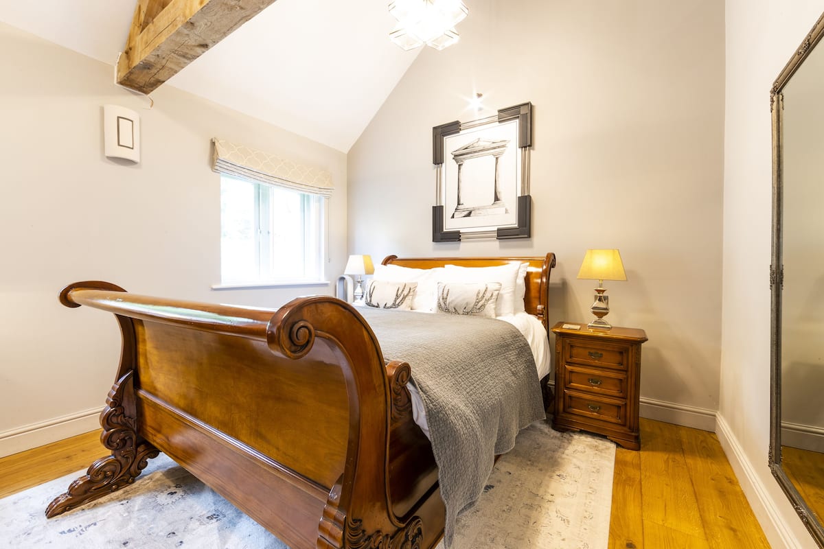 Um quarto com cama de madeira, mesa de cabeceira com abajur, janela com persianas e um quadro na parede.