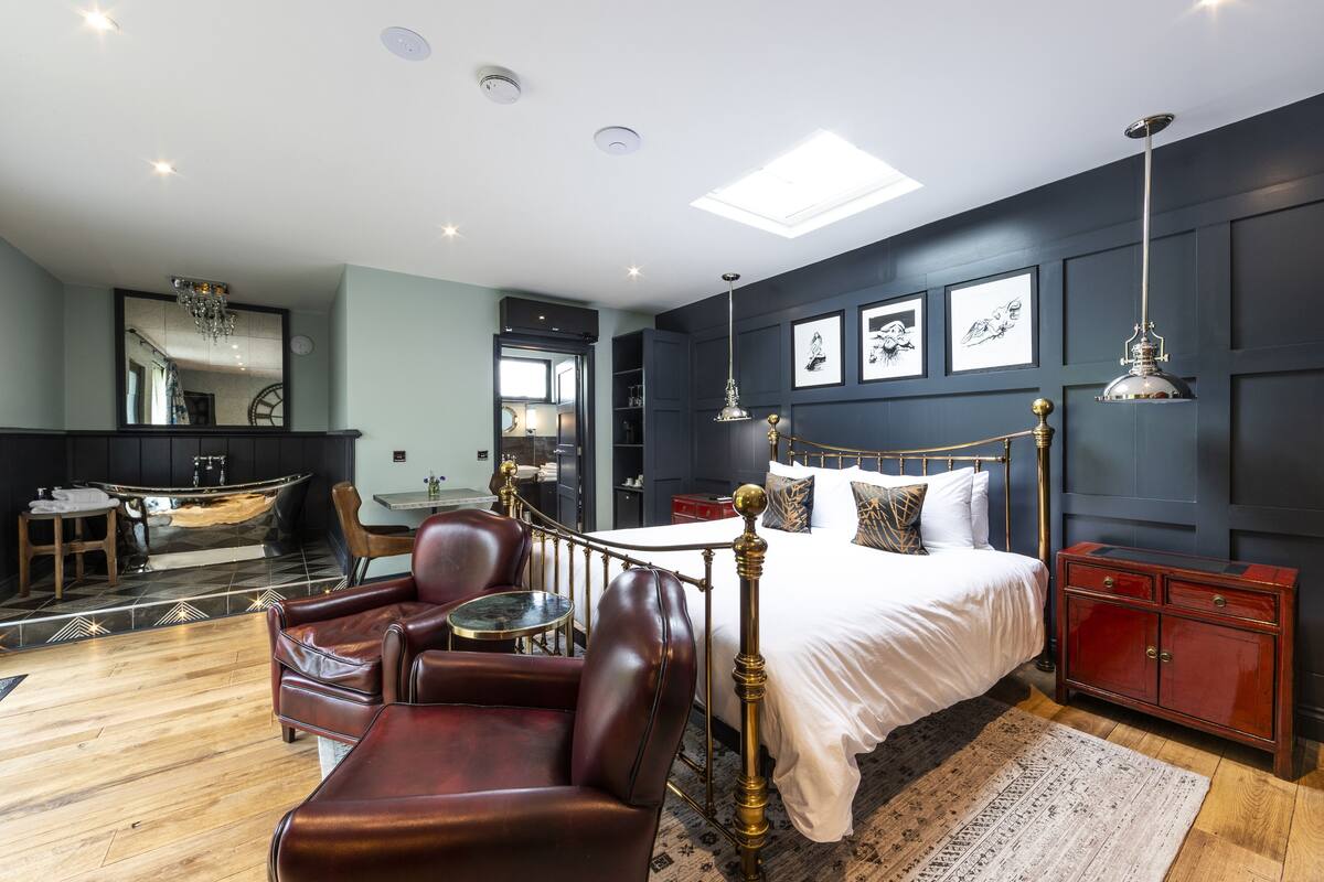 Quarto moderno com uma cama grande, poltronas de couro, uma mesinha e um armário vermelho.