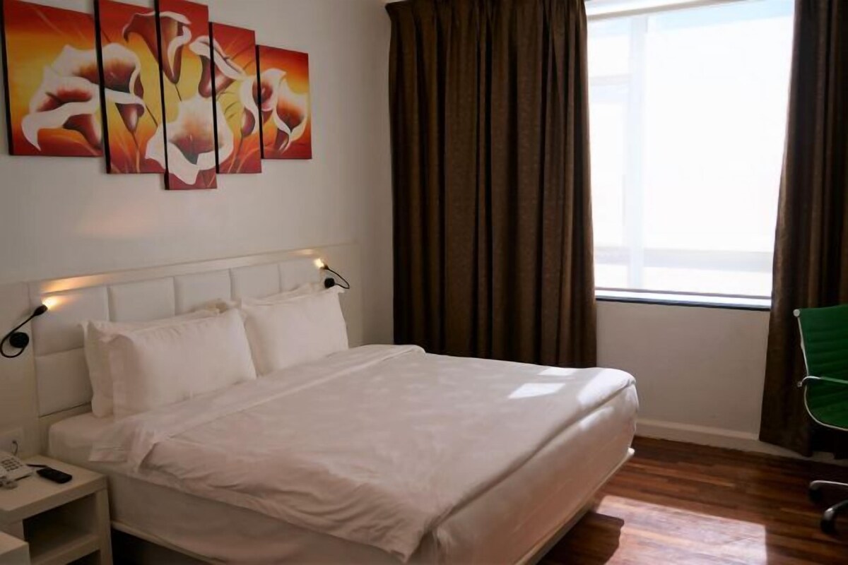 Quarto de hotel com cama, mesa de cabeceira, telefone e janela com cortinas.
