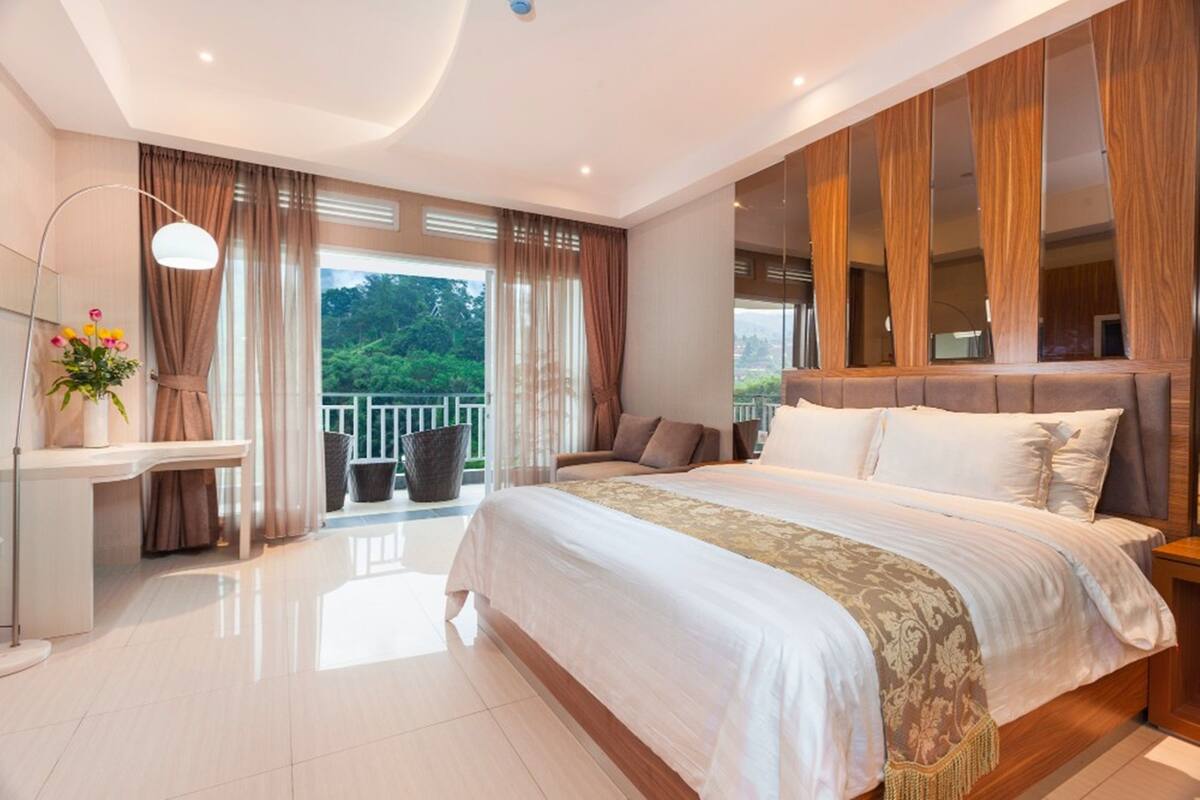 Quarto moderno com uma cama grande, uma mesa de cabeceira, um espelho e vista para o verde lá fora.