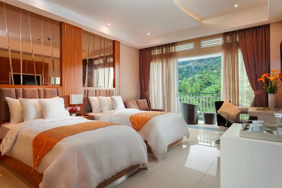 Quarto de hotel com duas camas, uma escrivaninha e vista para o exterior.
