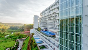 Um hotel moderno com vários andares, uma piscina no terraço e vista para um vale exuberante.