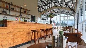 Interior de restaurante com balcão de madeira, banquetas de bar e uma grande janela com vista.