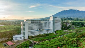 Um grande hotel com vários andares, rodeado por vegetação exuberante e uma montanha ao fundo.