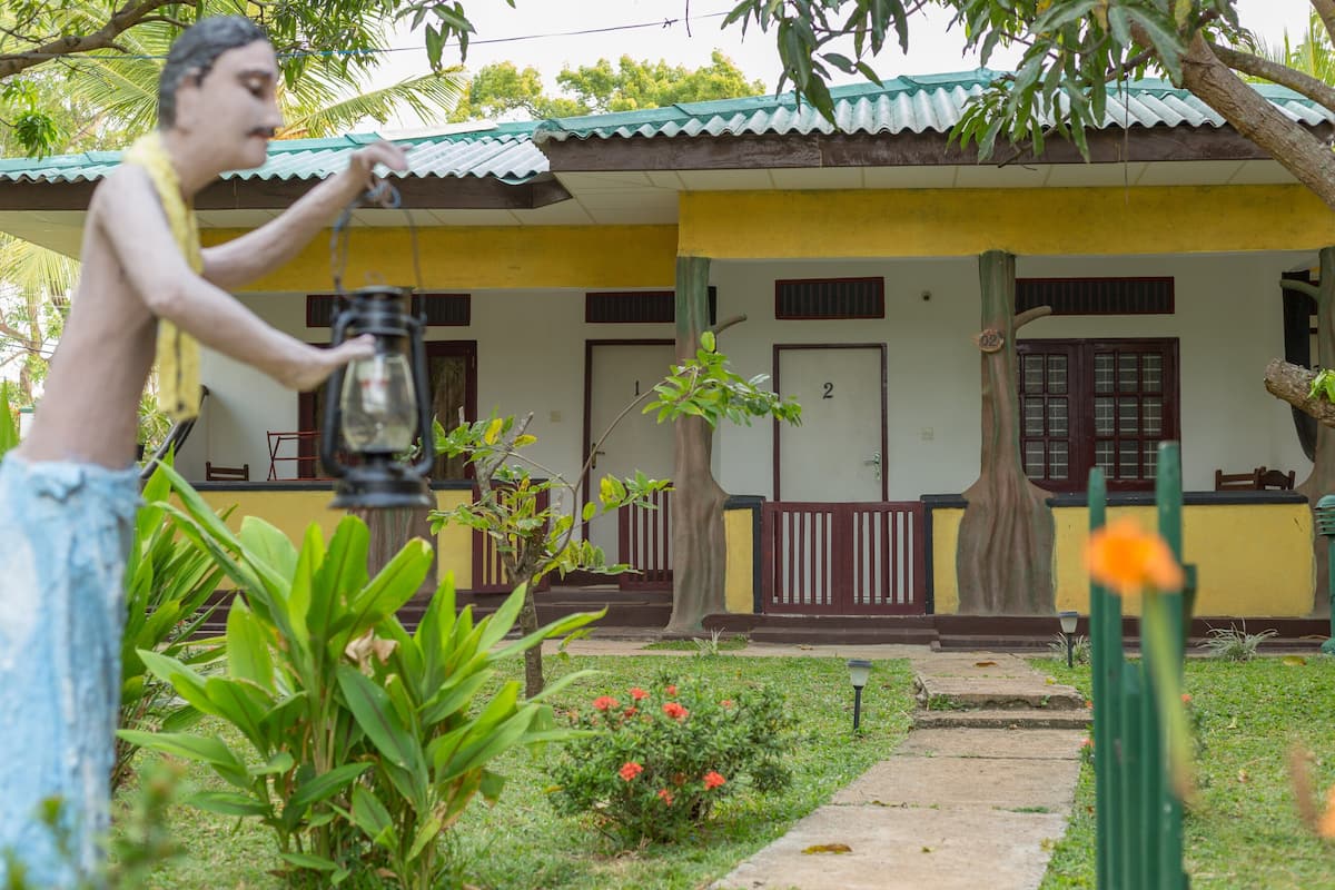 Um edifício amarelo com portas numeradas, varanda coberta e jardim com plantas e flores.