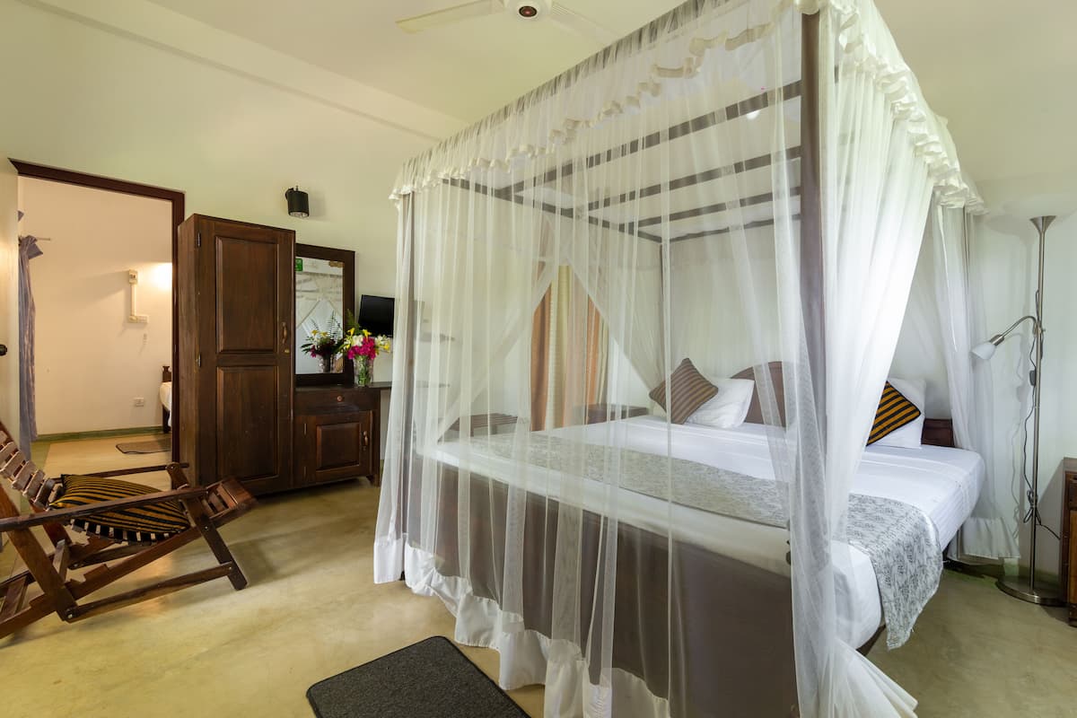 Quarto com cama de dossel, uma cadeira de balanço de madeira e mesa de cabeceira com abajur.