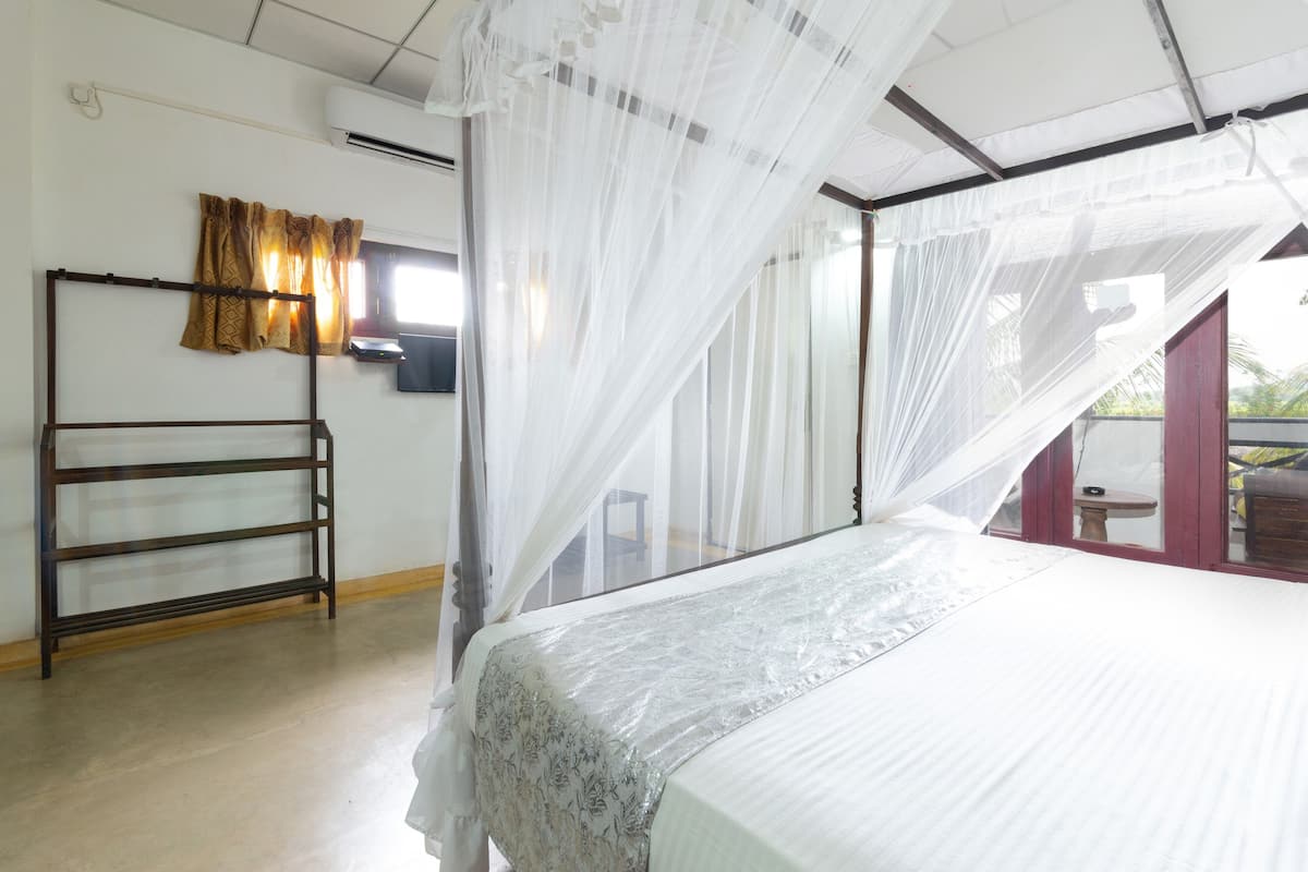 Quarto com cama, prateleira de madeira e mosquiteiro.