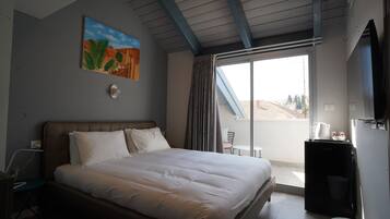 Quarto de hotel com cama, quadro, escrivaninha, cadeira, televisão e varanda com vista.