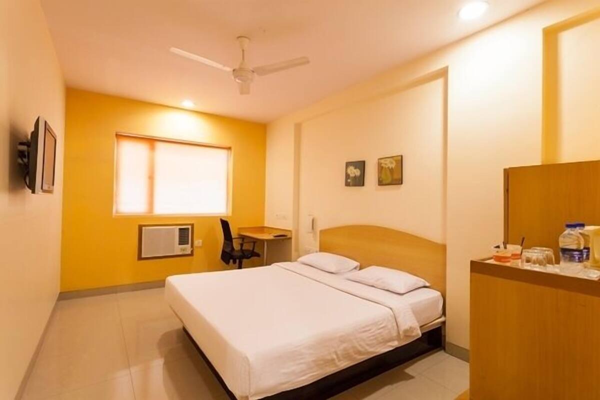 Quarto de hotel com cama, escrivaninha, cadeira, ventilador de teto e janela com persianas.
