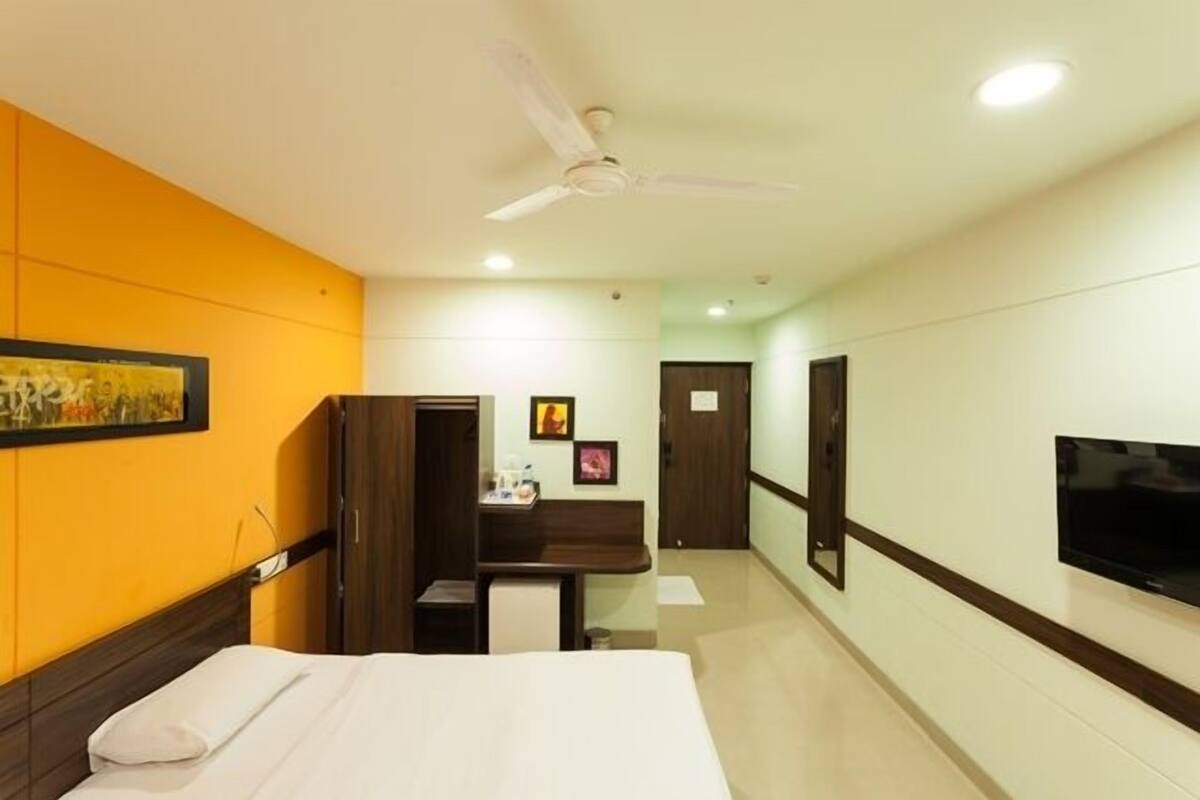Quarto de hotel com cama, escrivaninha, cadeira, televisão e ventoinha no teto.