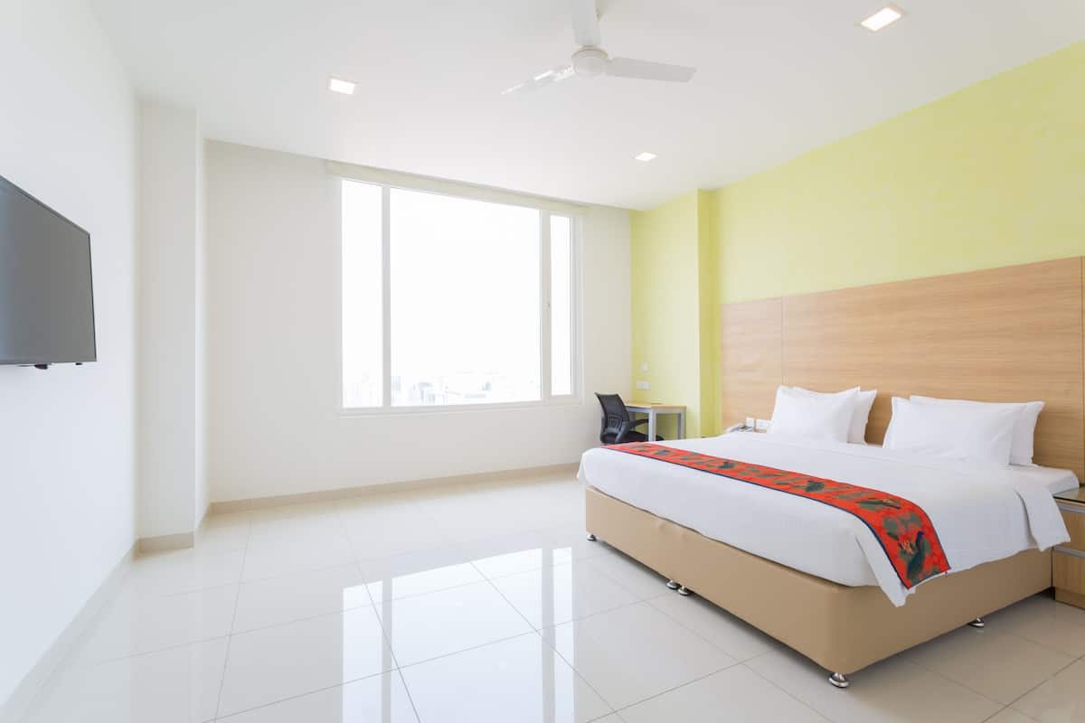 Quarto de hotel moderno com uma cama grande, televisão de tela plana, ventilador de teto e uma grande janela que proporciona luz natural.