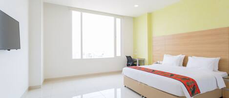 Quarto de hotel moderno com uma cama grande, televisão de tela plana, ventilador de teto e uma grande janela que proporciona luz natural.