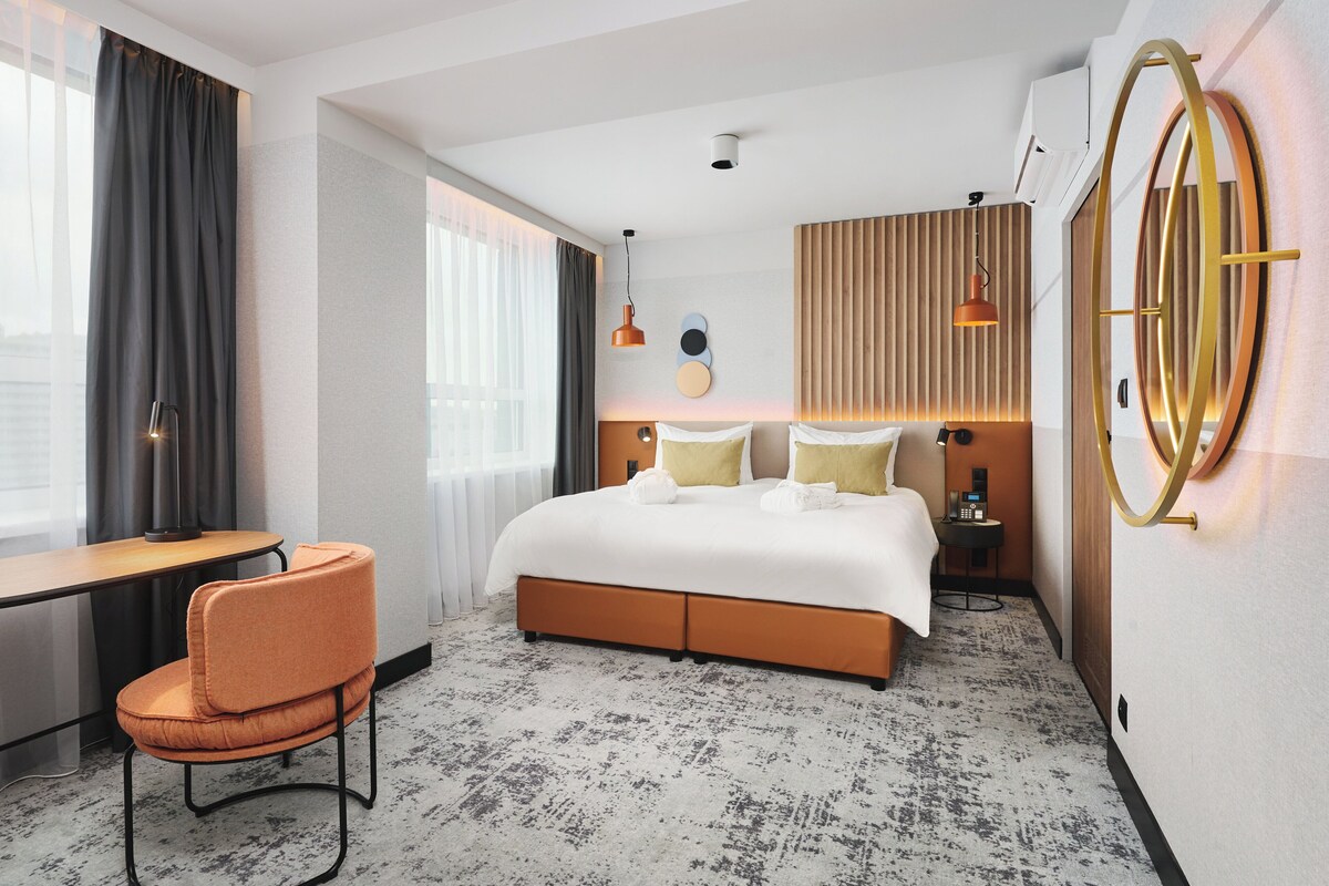 Quarto de hotel moderno com uma cama grande, uma escrivaninha e uma cadeira.