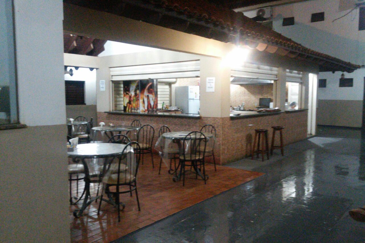 Um restaurante com mesas, cadeiras, um balcão e piso ladrilhado.