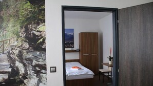 Quarto com cama, guarda-roupa de madeira, escrivaninha com cadeira e um quadro na parede.