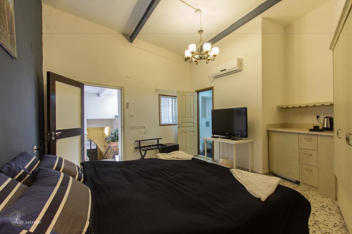 Quarto com cama, televisão, escrivaninha e cozinha compacta.