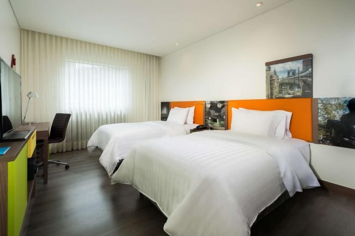 Quarto de hotel com duas camas, uma escrivaninha e uma cadeira.