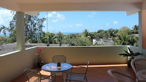Uma varanda com mesa redonda e cadeiras, com vista para o oceano e vegetação.