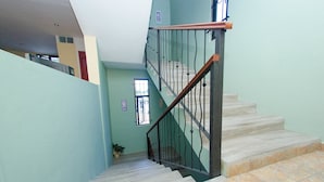 Uma escadaria com corrimão de metal e degraus de pedra, conduzindo a um andar superior.