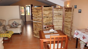 Uma sala de jantar com mesa e cadeiras de madeira, um modelo de navio na mesa e uma cadeira com almofada.