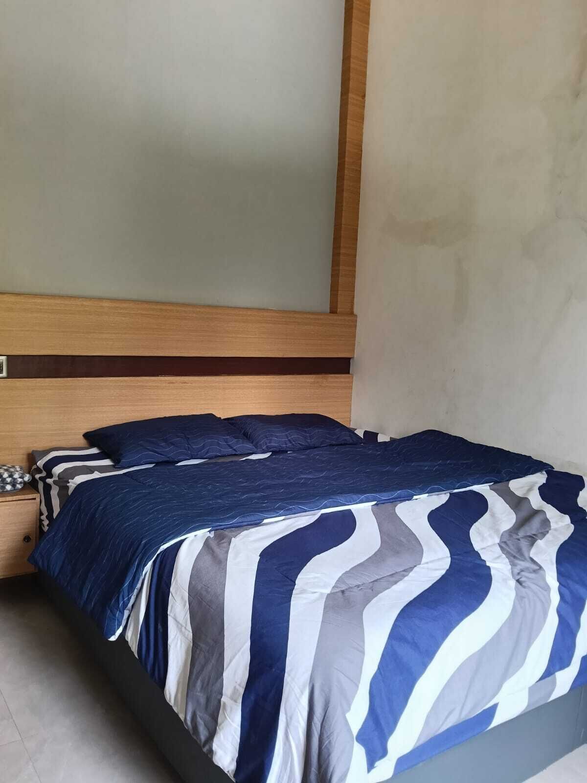 Quarto com cama, cabeceira de madeira e mesa de cabeceira com abajur.