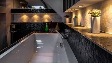 Uma casa de banho moderna com uma banheira grande, parede com textura de pedra e iluminação embutida.