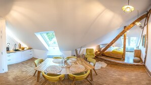 Uma sala de jantar com mesa de madeira e cadeiras amarelas, uma cozinha com armários brancos e um quarto no mezanino com escada de madeira.