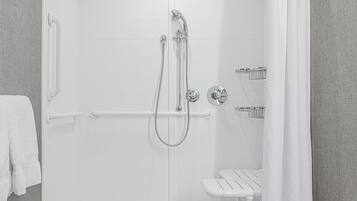 Um chuveiro sem barreiras com porta de vidro, um chuveiro manual, um suporte para toalhas e um vaso sanitário.