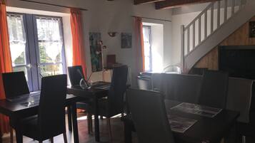 Uma área de refeições com mesa e cadeiras de madeira, um radiador e uma escada que dá para outro andar.