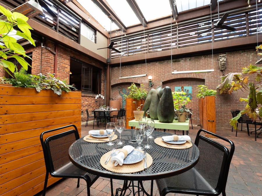 Restaurante com mesas ao ar livre, paredes de tijolo e plantas penduradas.