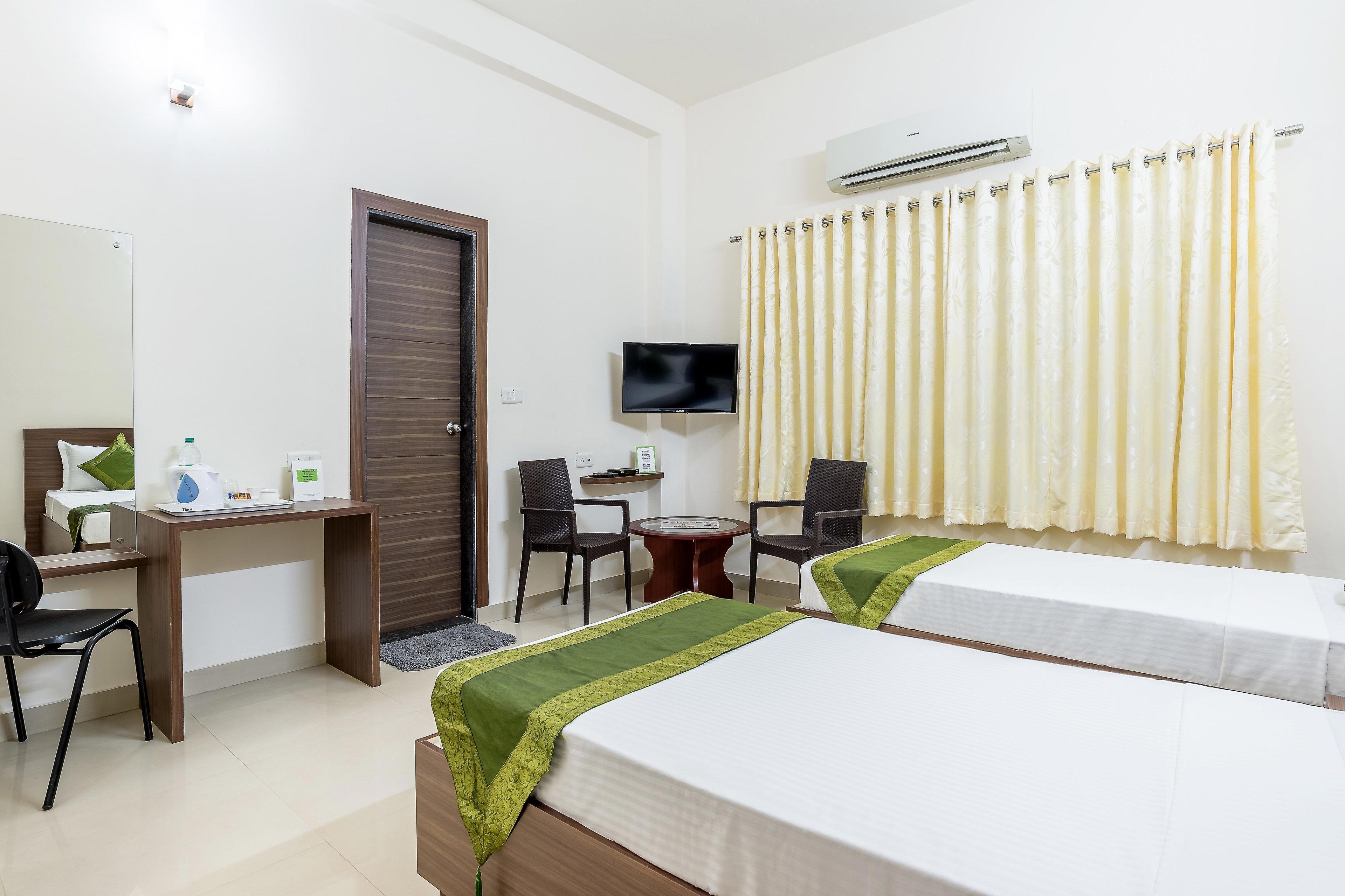 Quarto de hotel com duas camas, uma escrivaninha, uma cadeira, uma televisão e um aparelho de ar condicionado.