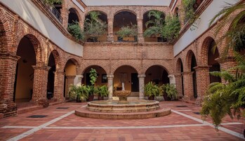 Pátio com uma fonte central, rodeado por arcos de tijolo e vasos de plantas.