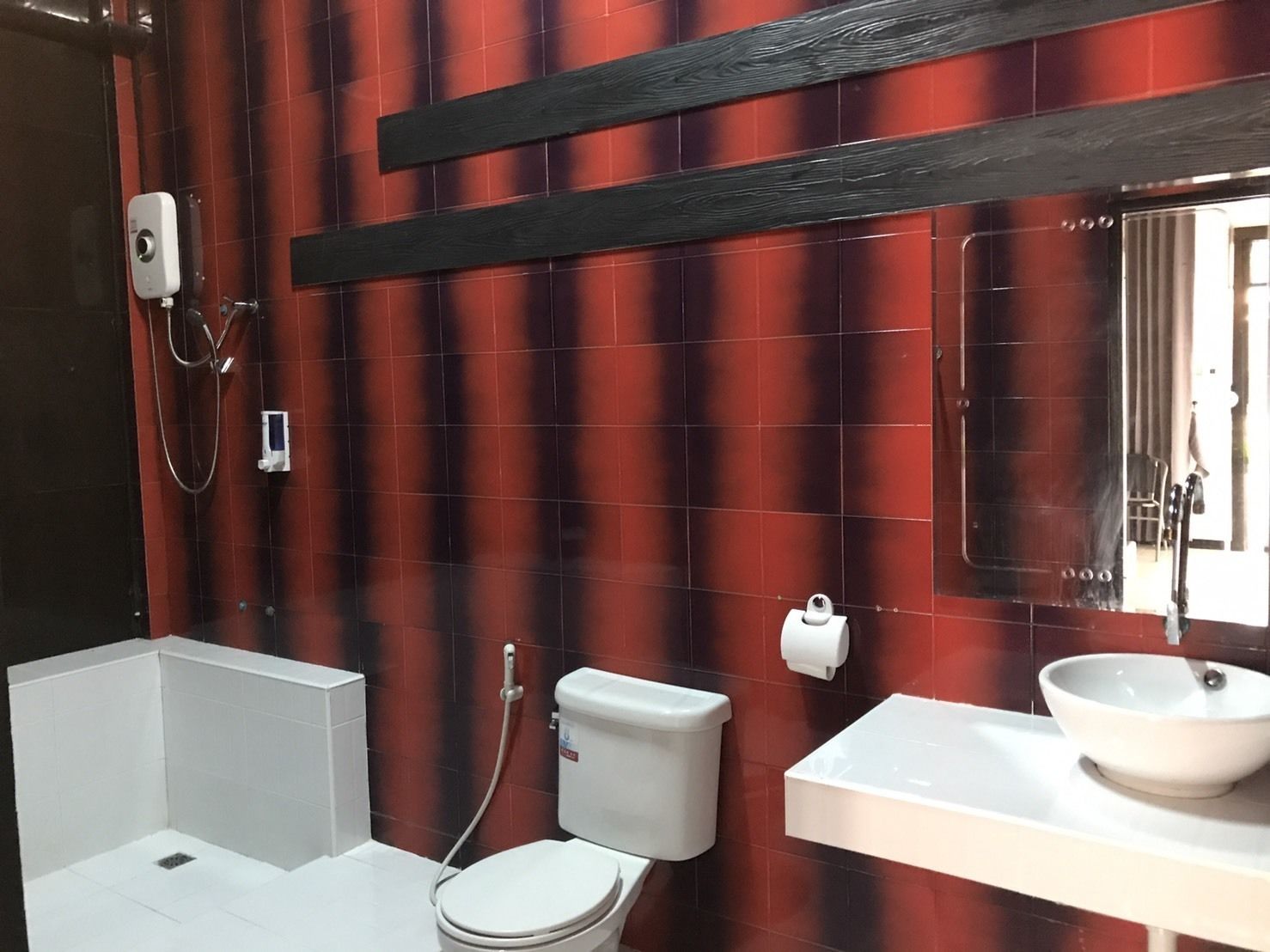 Um banheiro com parede revestida em azulejos vermelhos, vaso sanitário branco, pia branca com cuba e espelho sobre a pia.
