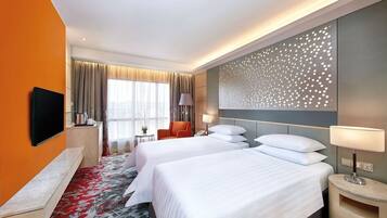 Quarto de hotel com duas camas, televisão, escrivaninha e um painel decorativo na parede.