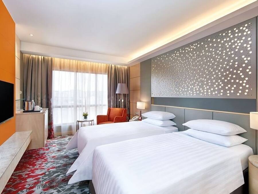 Quarto de hotel com duas camas, televisão, escrivaninha e um painel decorativo na parede.