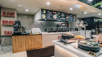 Um balcão de café da manhã moderno com máquina de café, diversas opções de comida e um quadro de cardápio.
