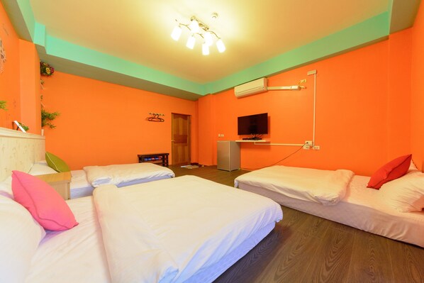 Quarto de hotel com quatro camas, ar condicionado, televisão e uma pequena mesa com uma planta.