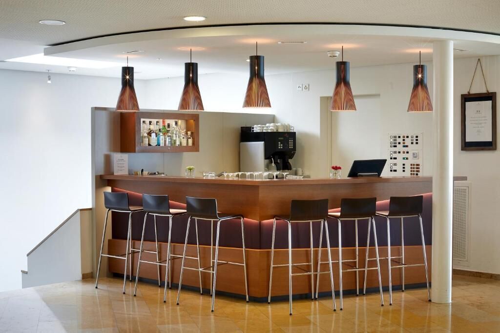 Uma área de bar moderna com balcão curvo, banquetas e iluminação pendente.