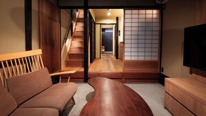 Um interior japonês tradicional, com escada de madeira, tatames e uma mesa de madeira baixa, além de uma televisão.