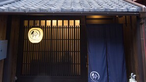 Um edifício tradicional japonês com telhado de telhas, porta de madeira com sistema deslizante e cortina azul.