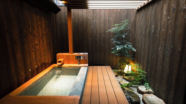 Uma área de spa com madeira, incluindo uma banheira de hidromassagem, um deck de madeira e um pequeno jardim com pedras e plantas.