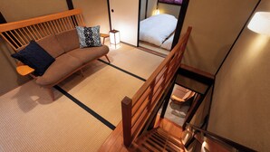 Quarto em estilo japonês tradicional, com tatames, cama de madeira baixa, sofá com almofadas e uma mesinha com abajur.